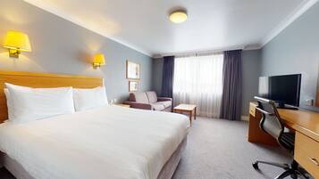 Quarto de hotel com uma cama grande, uma escrivaninha com cadeira, uma televisão e duas luminárias na parede.
