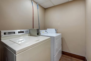 Uma lavanderia com máquina de lavar e secadora Maytag para uso comercial, painel de controle e tubulação de água.
