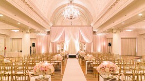 Um salão imponente com fileiras de cadeiras e um corredor central, provavelmente para um casamento ou evento formal.