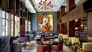 Um hall amplo com um grande candelabro, área de bar e disposição de mesas e cadeiras.