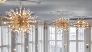 Um quarto com grandes janelas, lustres elegantes e detalhes arquitetônicos clássicos.