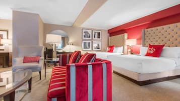 Quarto de hotel com cama, sofá, poltrona, escrivaninha e luminária.
