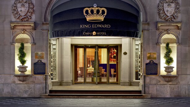 Entrada do Hotel King Edward Omni com logotipo de coroa, arquitetura clássica e uma escadaria imponente.
