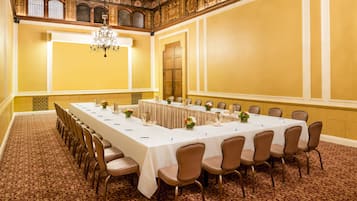 Uma sala de conferências com uma mesa comprida, cadeiras, um candelabro e detalhes ornamentais no teto.