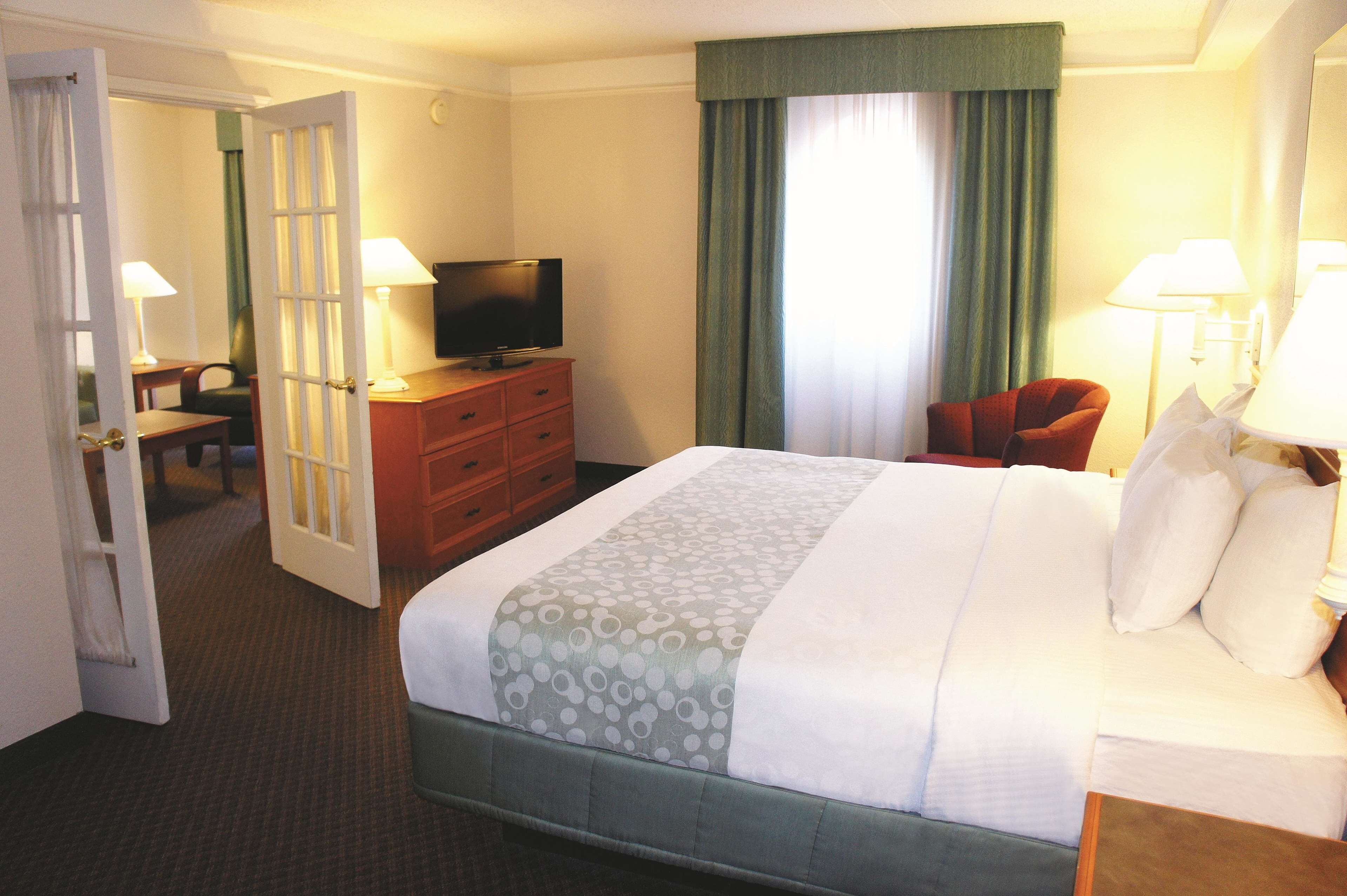 Quarto de hotel com uma cama, televisão, escrivaninha com cadeira e janela com cortinas.