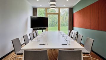 Uma sala de conferências com uma mesa comprida, cadeiras, uma TV de tela plana e vista para o verde através de grandes janelas.