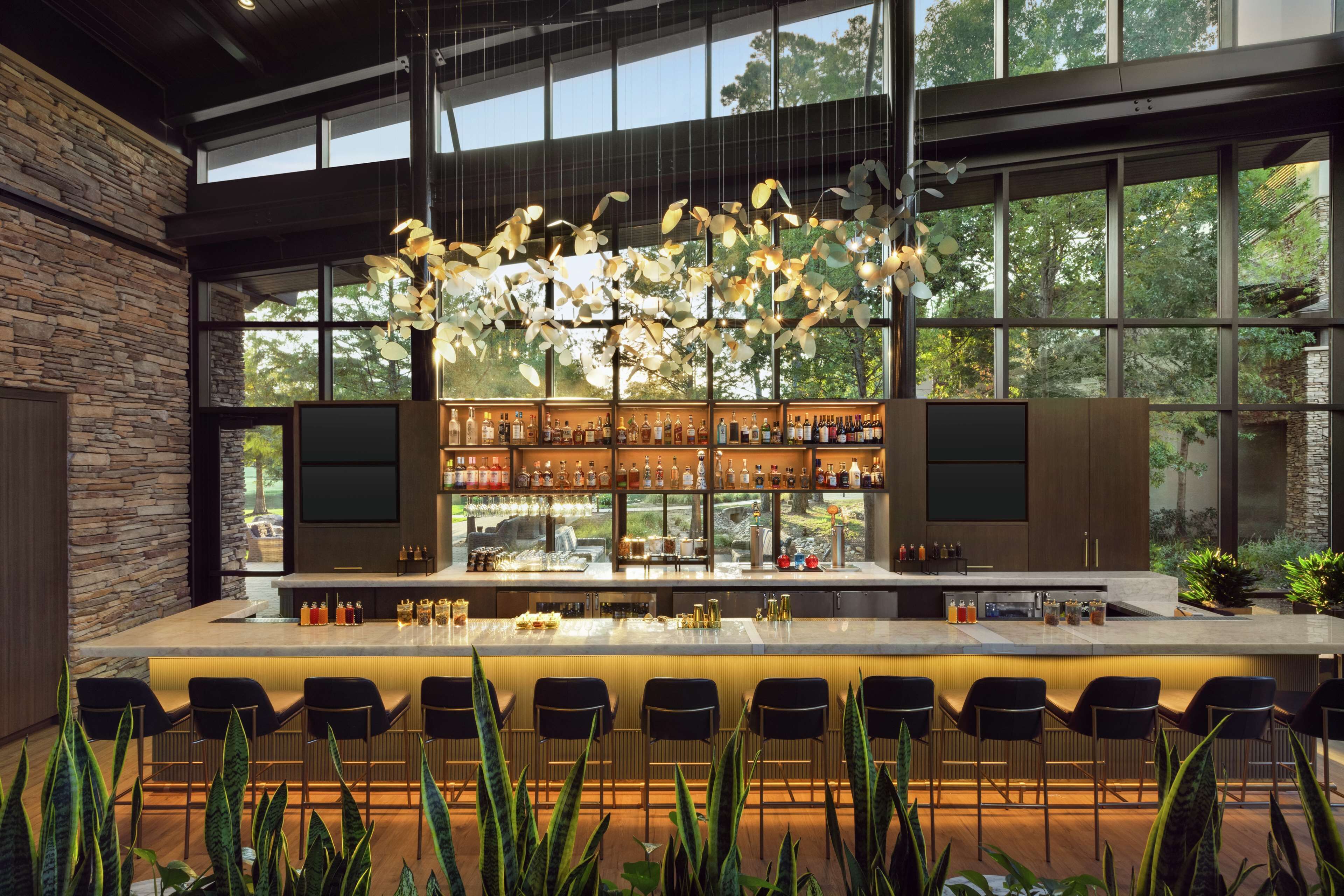 Uma área de bar moderna, com um balcão comprido, diversas opções de assento e uma grande janela com vista para o exterior.