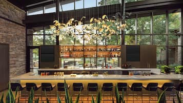 Uma área de bar moderna, com um balcão comprido, diversas opções de assento e uma grande janela com vista para o exterior.