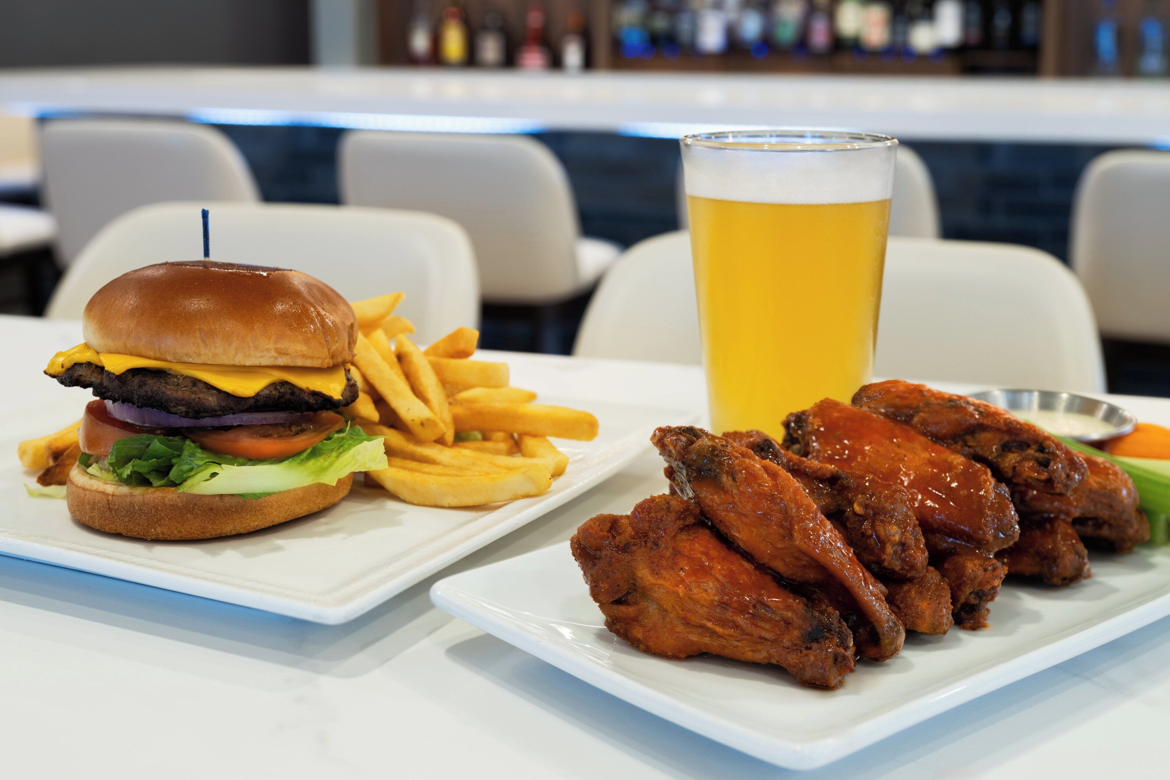 Uma refeição com hambúrguer, batatas fritas, asas de frango e um copo de cerveja em um prato branco.