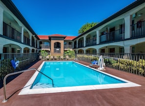 Piscina com calçada ao redor, edifício com varandas e céu azul límpido.