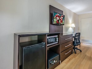 Quarto de hotel com secretária, micro-ondas, cofre, cadeira e televisão na parede.