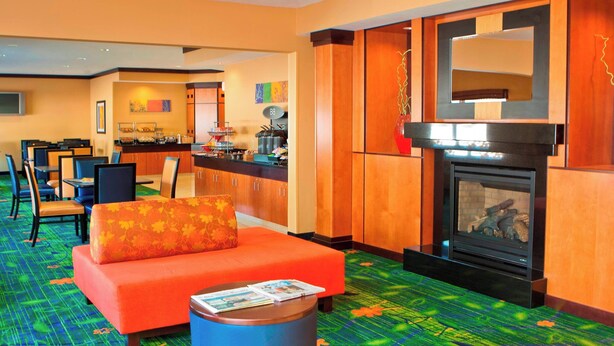 Um lobby de hotel com um sofá, uma mesinha, uma lareira e uma área de cozinha ao fundo.