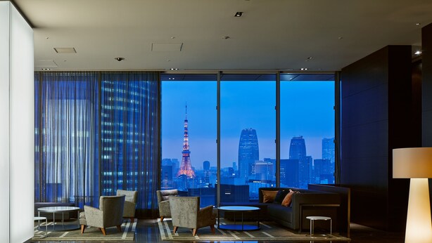 Um saguão de hotel moderno com uma ampla janela panorâmica que oferece vista para o horizonte urbano, incluindo uma torre imponente.