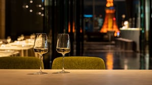 Duas taças de vinho vazias sobre uma mesa em um restaurante com pouca luz, com vista para o horizonte da cidade ao fundo.