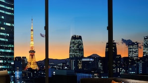 Vista da cidade a partir de um quarto de hotel, com uma janela grande, mostrando edifícios iluminados e uma torre imponente.