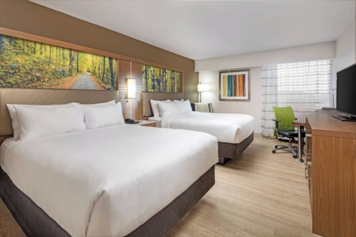 Quarto de hotel com duas camas, uma mesa, uma cadeira e obras de arte nas paredes.