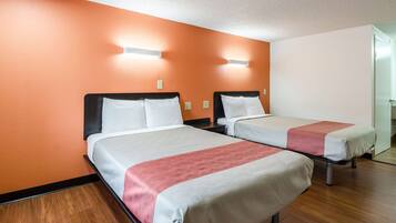 Quarto de hotel com duas camas, paredes laranja e chão de madeira.