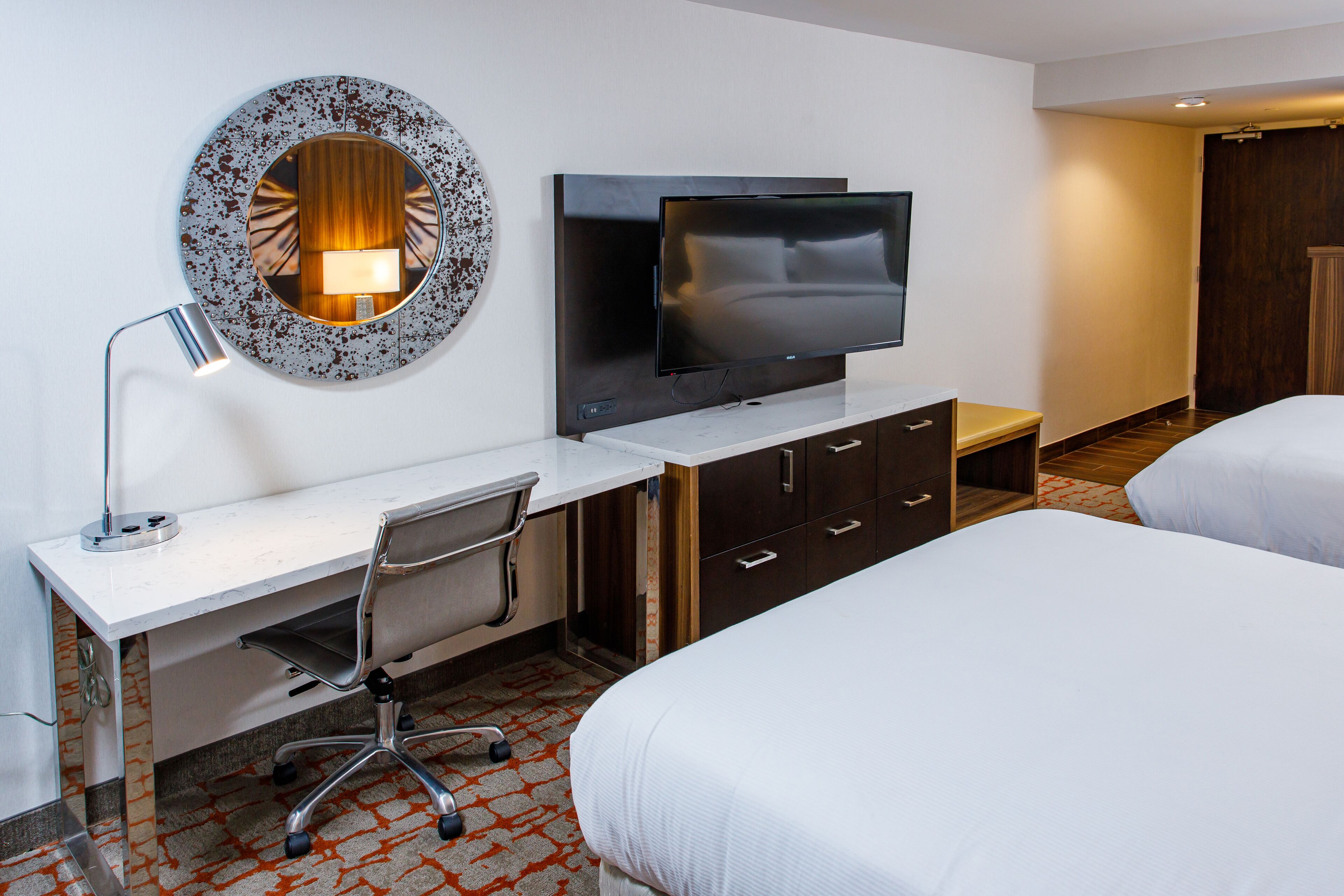Quarto de hotel com televisão de tela plana, uma escrivaninha com cadeira e duas camas.