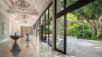 Um corredor amplo com grandes janelas, lustres modernos e vista para um jardim exuberante.