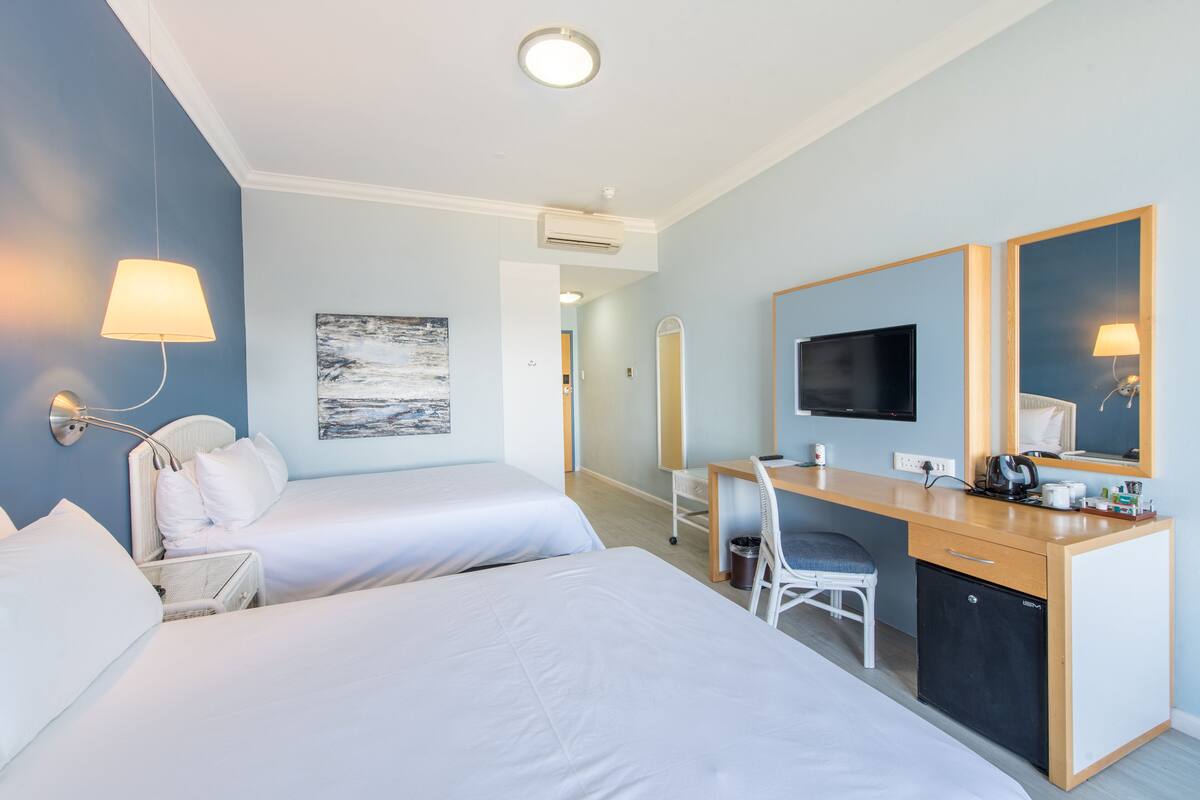 Quarto de hotel com duas camas, uma escrivaninha, uma cadeira, uma televisão e banheiro.