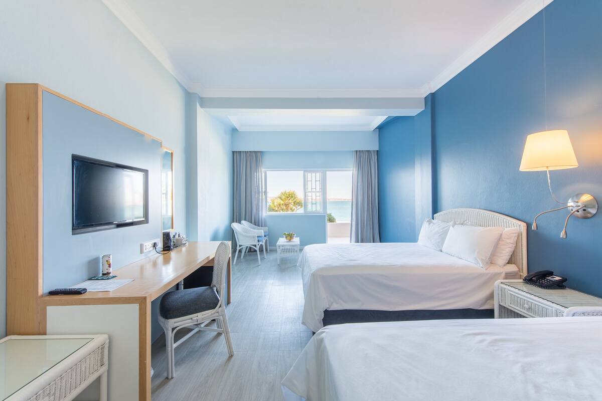Quarto de hotel com cama, escrivaninha, cadeira, televisão e vista para o exterior.