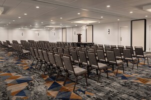 Sala de conferências com fileiras de cadeiras, um púlpito e piso coberto por carpete.