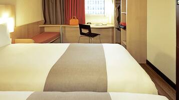 Quarto de hotel com duas camas, uma escrivaninha, uma cadeira, uma janela com cortinas e um guarda-roupa.