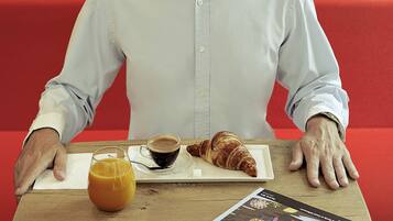Uma pessoa sentada à mesa com um croissant, uma xícara de café e um copo de suco de laranja.