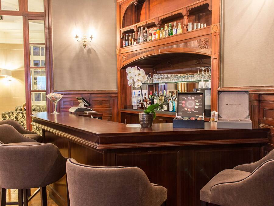 Uma área de bar com balcão de madeira, banquetas, um minibisco e uma variedade de garrafas e copos.