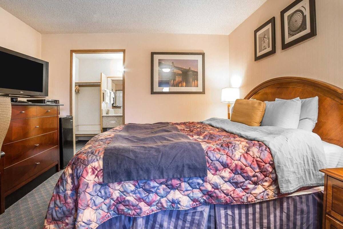 Quarto de hotel com cama, cômoda, televisão e quadros na parede.