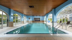 Piscina interna com paredes de vidro transparente, teto de madeira e chão de azulejos.