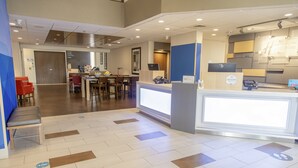 Uma área de recepção de hotel com design moderno, incluindo balcão de atendimento, espaço de estar e vista para o saguão.