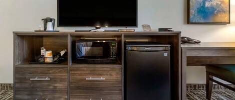 Quarto de hotel compacto com televisão de tela plana, micro-ondas, mini-geladeira, escrivaninha e uma cadeira.