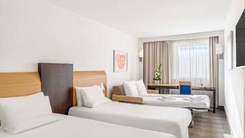 Quarto de hotel com duas camas, uma escrivaninha, uma cadeira, televisão e janela com cortinas.