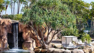 Uma cascata desemboca numa piscina rodeada por pedras e vegetação tropical.