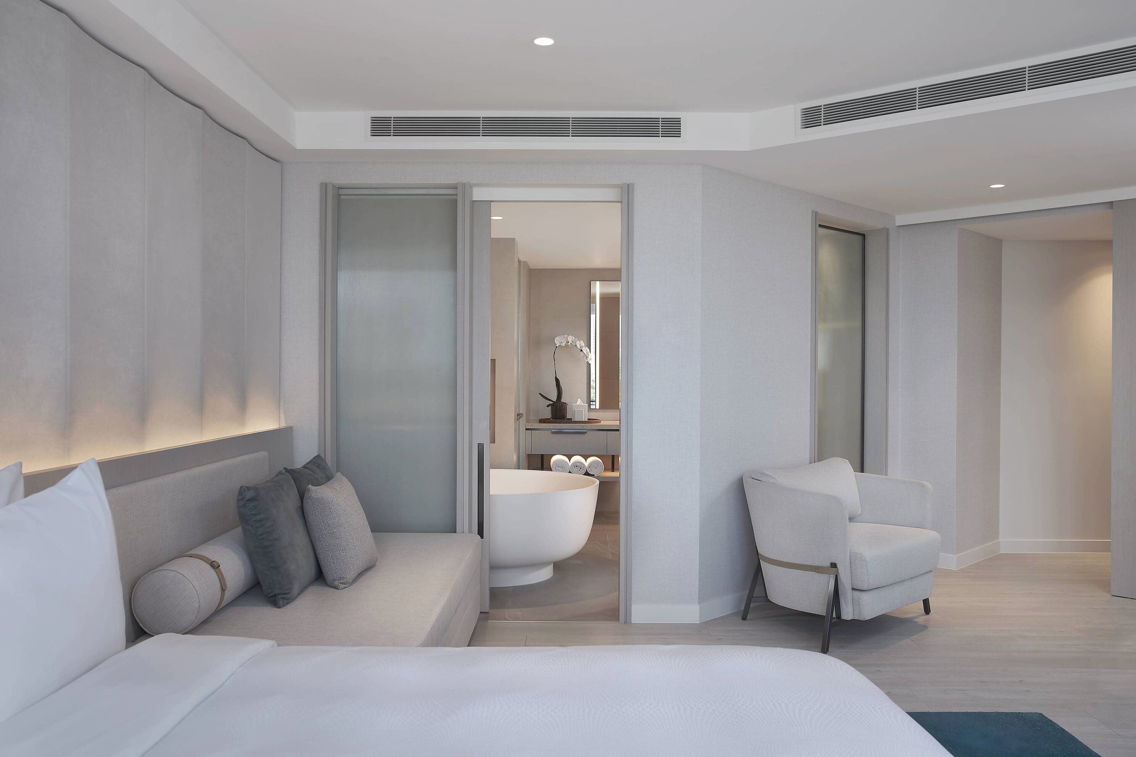 Quarto de hotel moderno com uma cama grande, área de estar, banheira e uma cadeira.