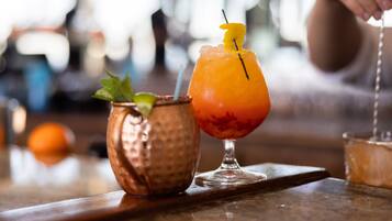 Dois cocktails sobre o balcão de um bar, um em um copo de cobre e outro em um copo com canudo.