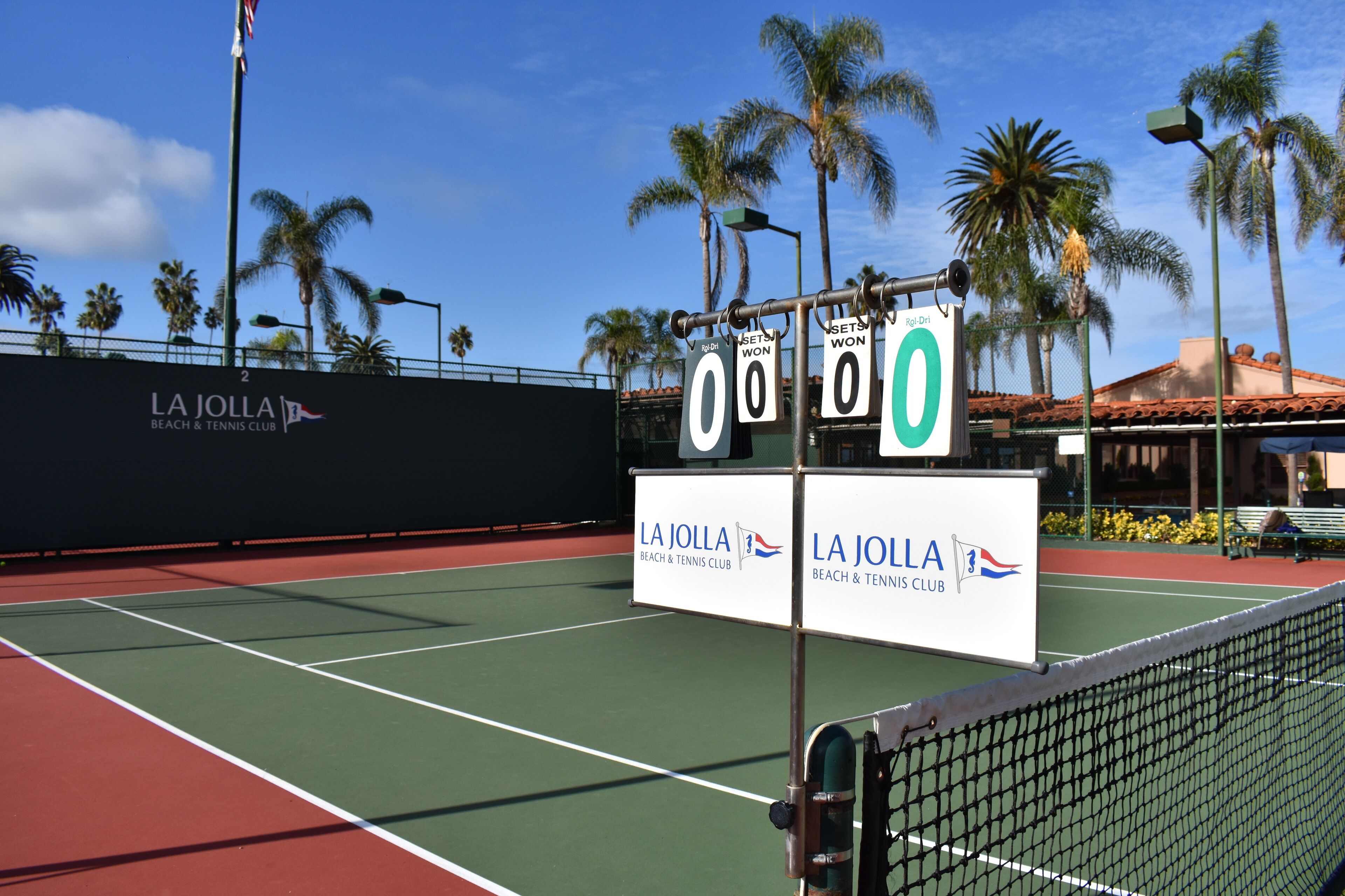 Uma quadra de tênis com rede, palmeiras e uma placa para o La Jolla Beach & Tennis Club.