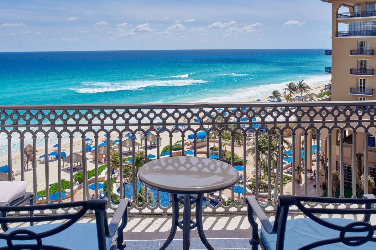 Varanda com mesa e cadeiras com vista para uma praia com guarda-sóis e espreguiçadeiras.