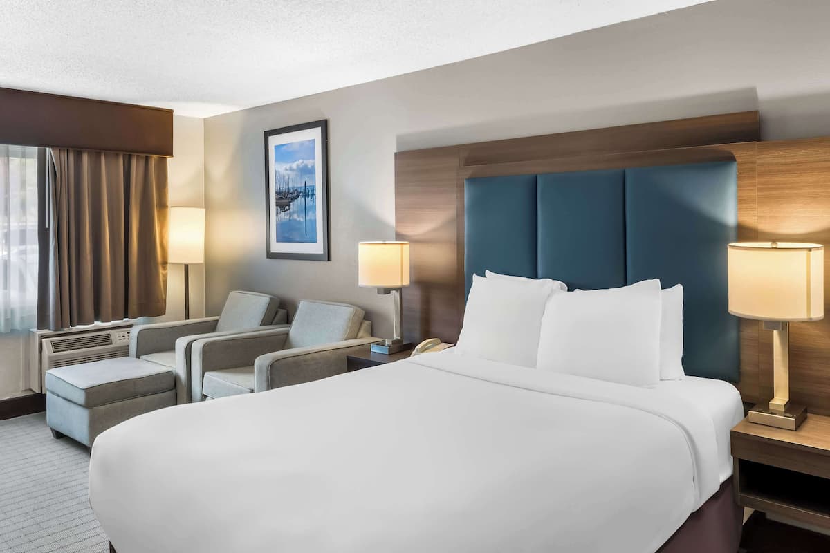 Quarto de hotel com uma cama grande, duas poltronas, um pequeno sofá, uma escrivaninha com abajur e um quadro na parede.