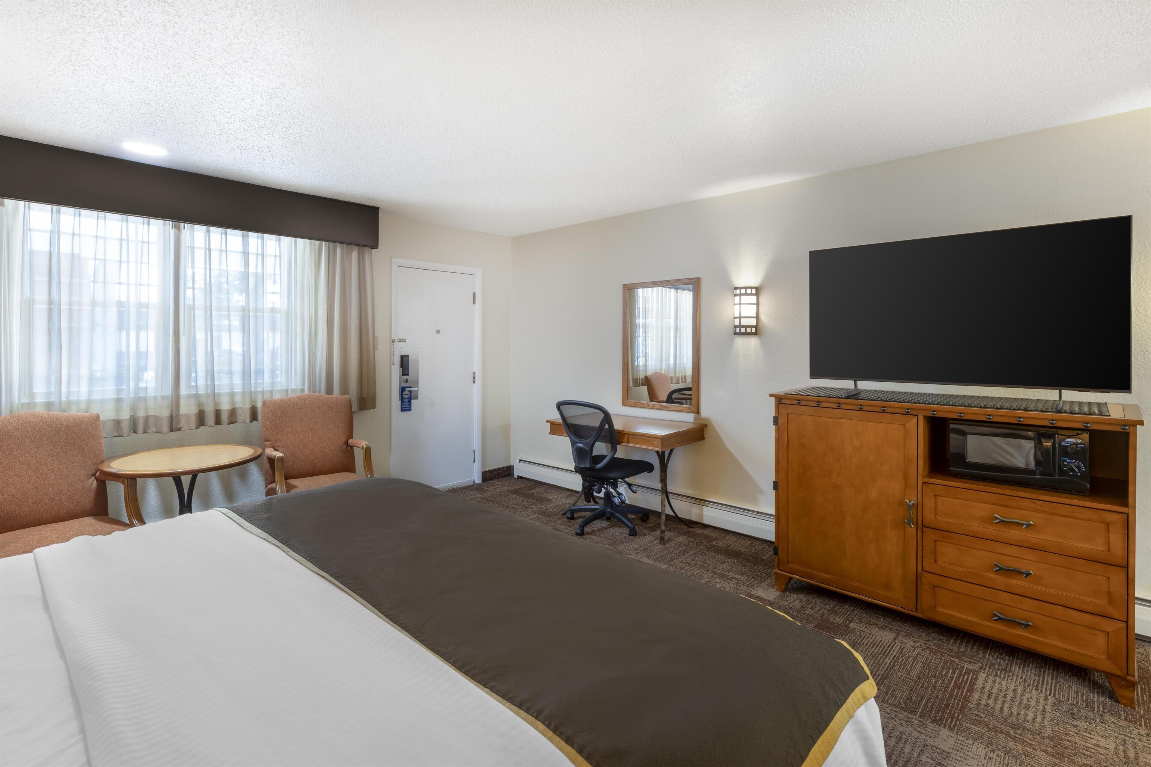 Quarto de hotel com cama, escrivaninha, cadeira, televisão e guarda-roupa.