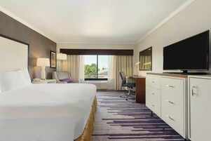 Quarto de hotel com uma cama grande, uma escrivaninha com cadeira, televisão e guarda-roupa.