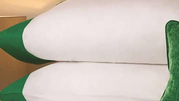 Uma cama com almofadas brancas e verdes, uma luminária e uma mesinha de cabeceira de madeira.