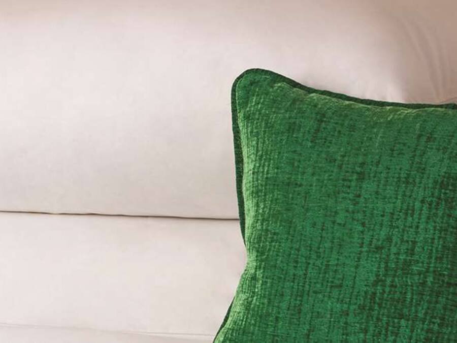Uma cama com almofadas brancas e verdes, uma luminária e uma mesinha de cabeceira de madeira.