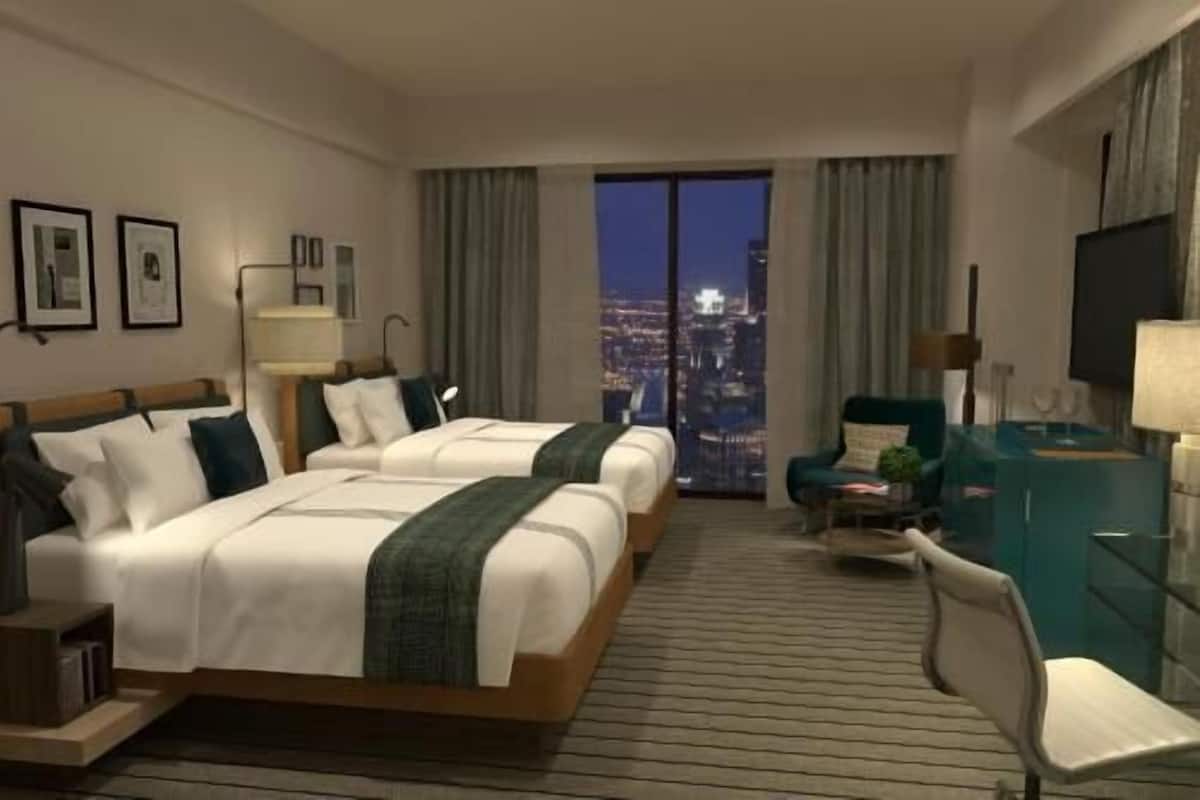 Quarto de hotel com duas camas, uma escrivaninha, uma cadeira, uma televisão e vista para a cidade.