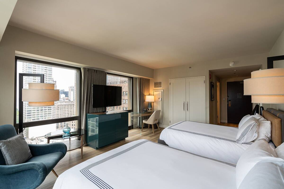 Quarto de hotel com duas camas, televisão, escrivaninha e vista para a cidade.