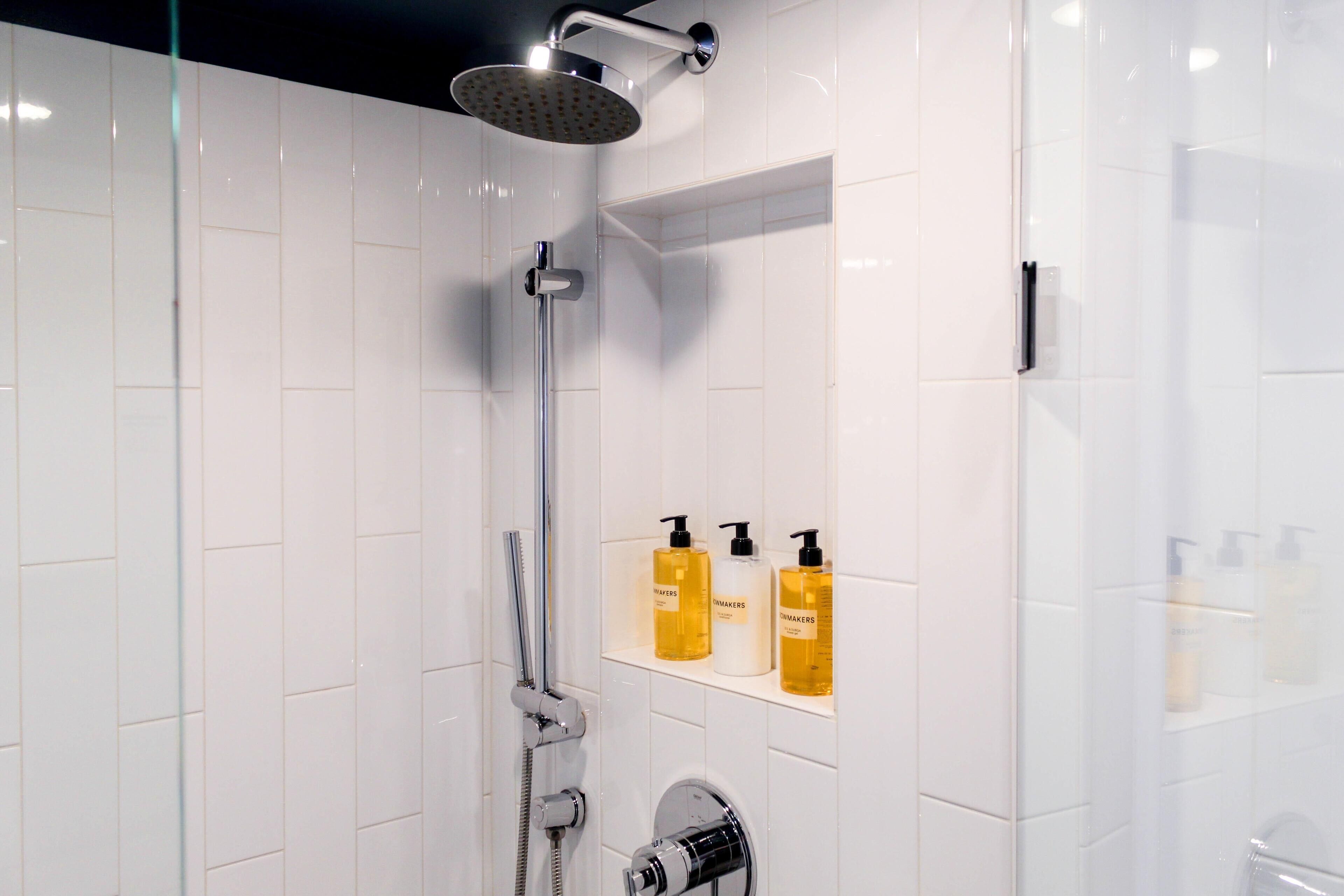 Um chuveiro moderno com chuveiro manual e torneira embutida na parede. Há três frascos de shampoo em uma prateleira.