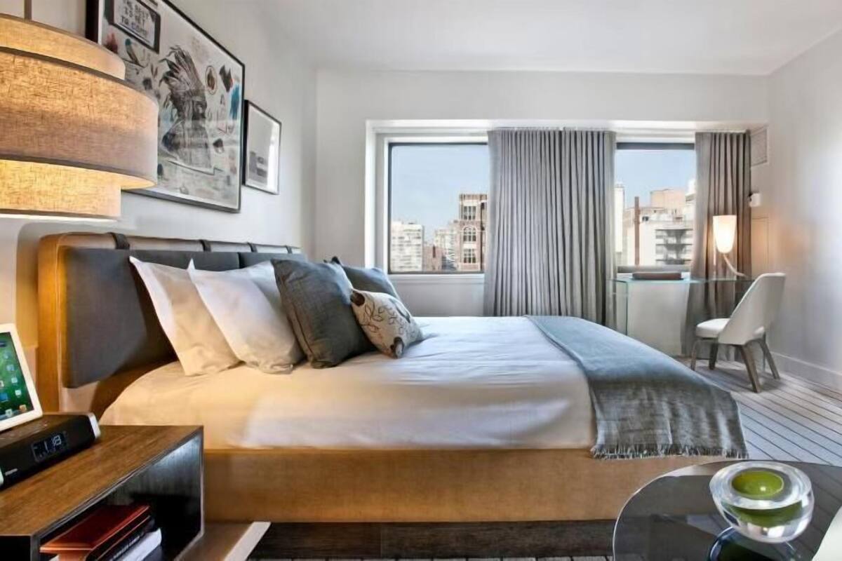 Quarto de hotel com cama, escrivaninha, televisão e janela com vista para a cidade.