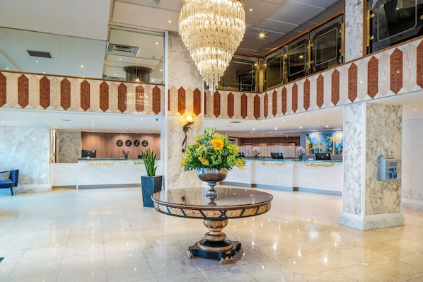 Um saguão com balcão de atendimento, um lustre e piso de mármore.