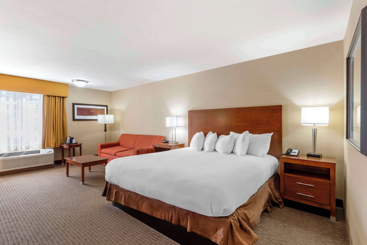 Quarto de hotel com uma cama grande, um sofá, uma escrivaninha e uma janela com cortinas.